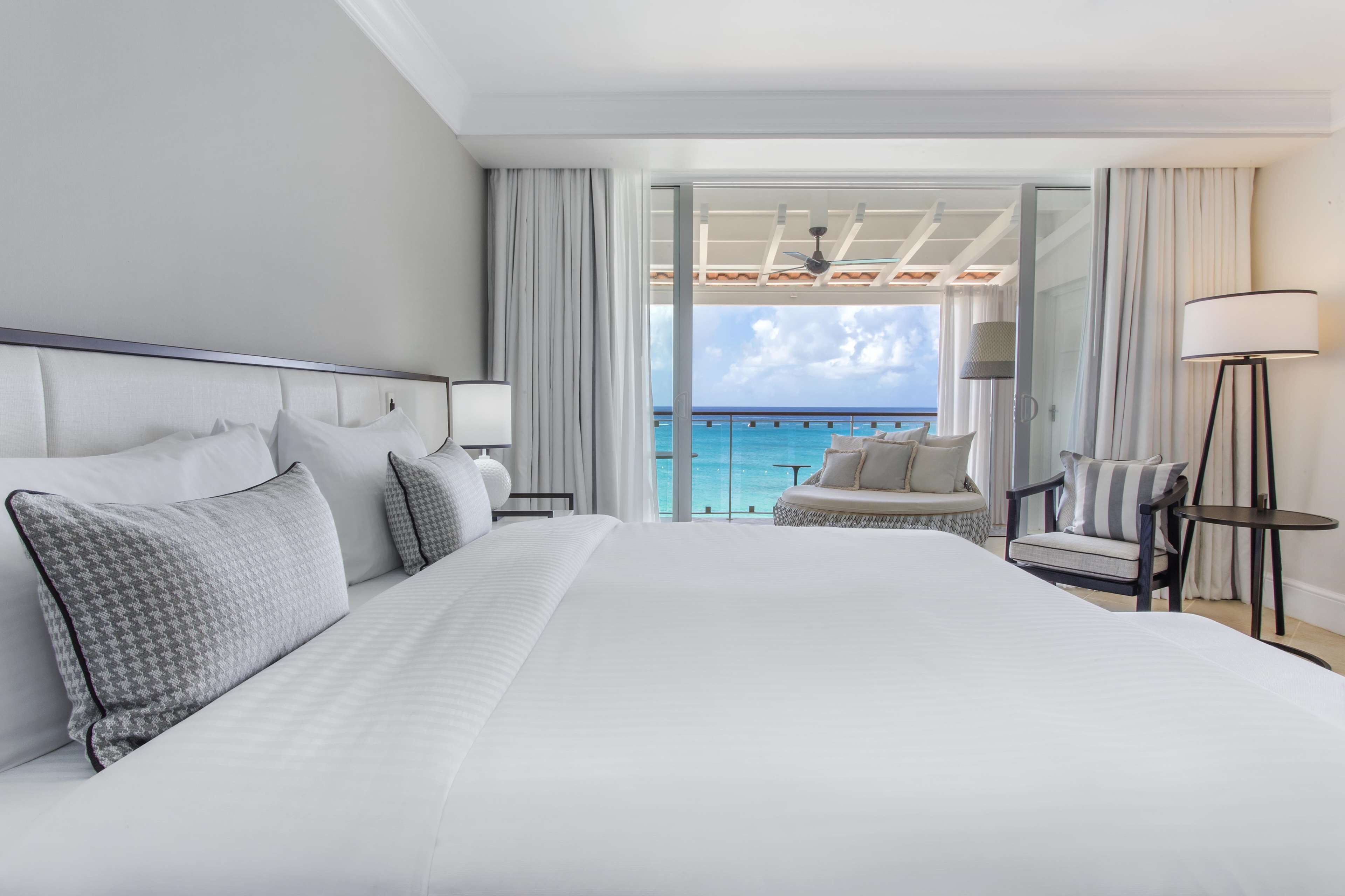 Quarto de hotel com uma cama grande, área de estar com vista para o oceano e uma varanda.