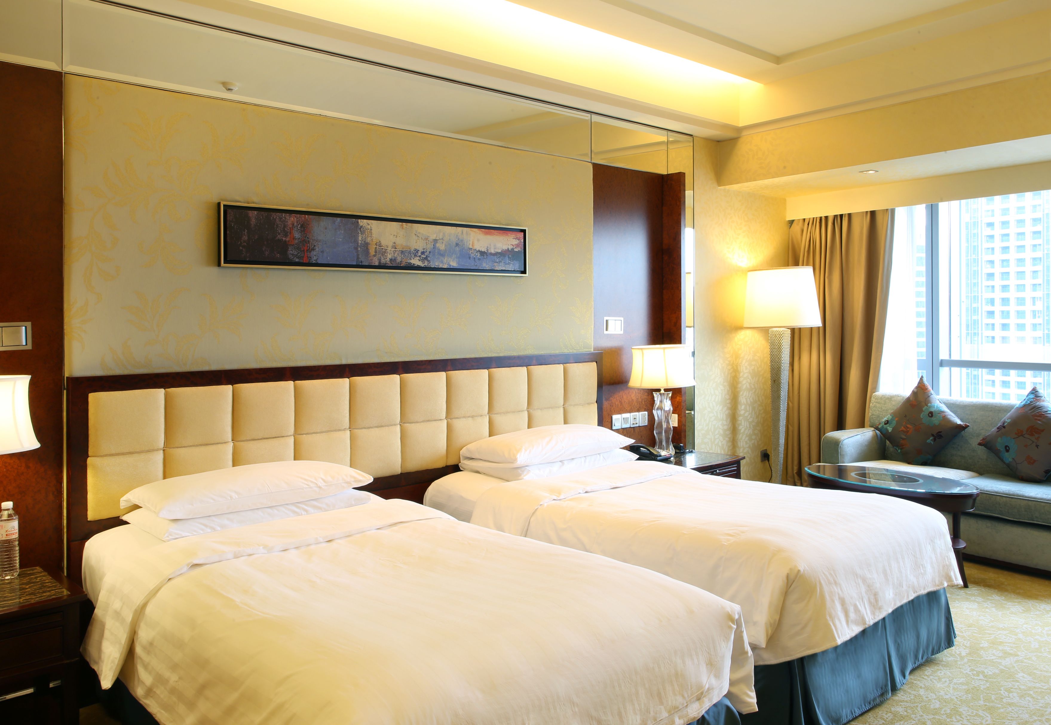 Quarto de hotel com duas camas, um sofá, uma TV e uma janela com cortinas.