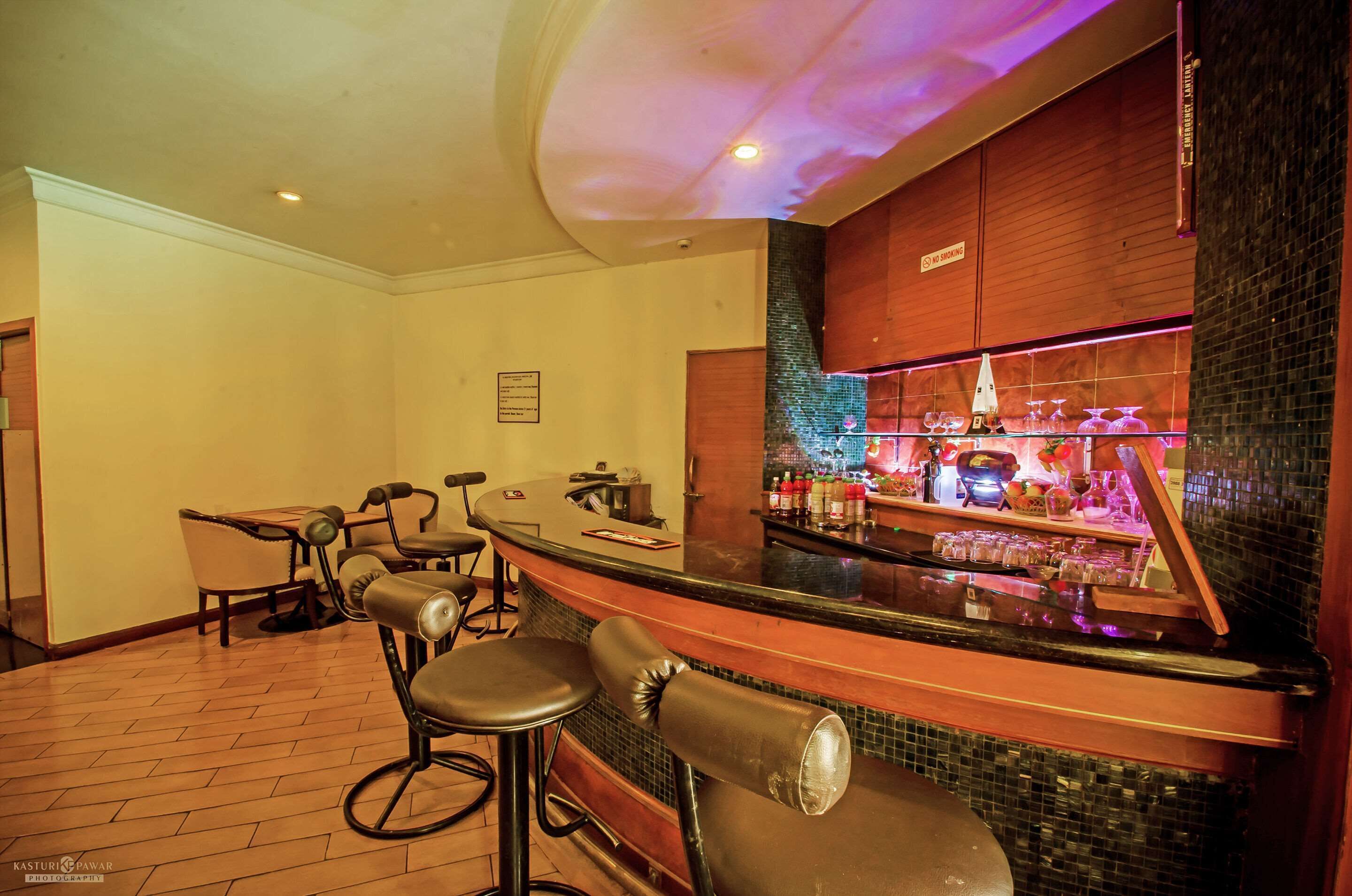 Uma área de bar com balcão curvo, banquetas e painel de azulejos.