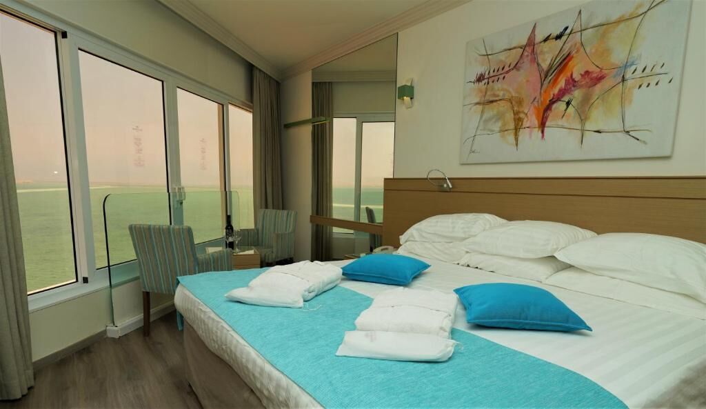 Quarto de hotel com cama, uma cadeira, uma janela grande e um quadro na parede.