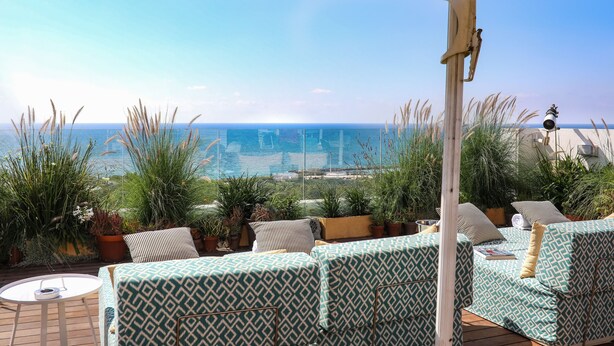 Terraço com área de estar ao ar livre, vasos de plantas e vista para o mar.