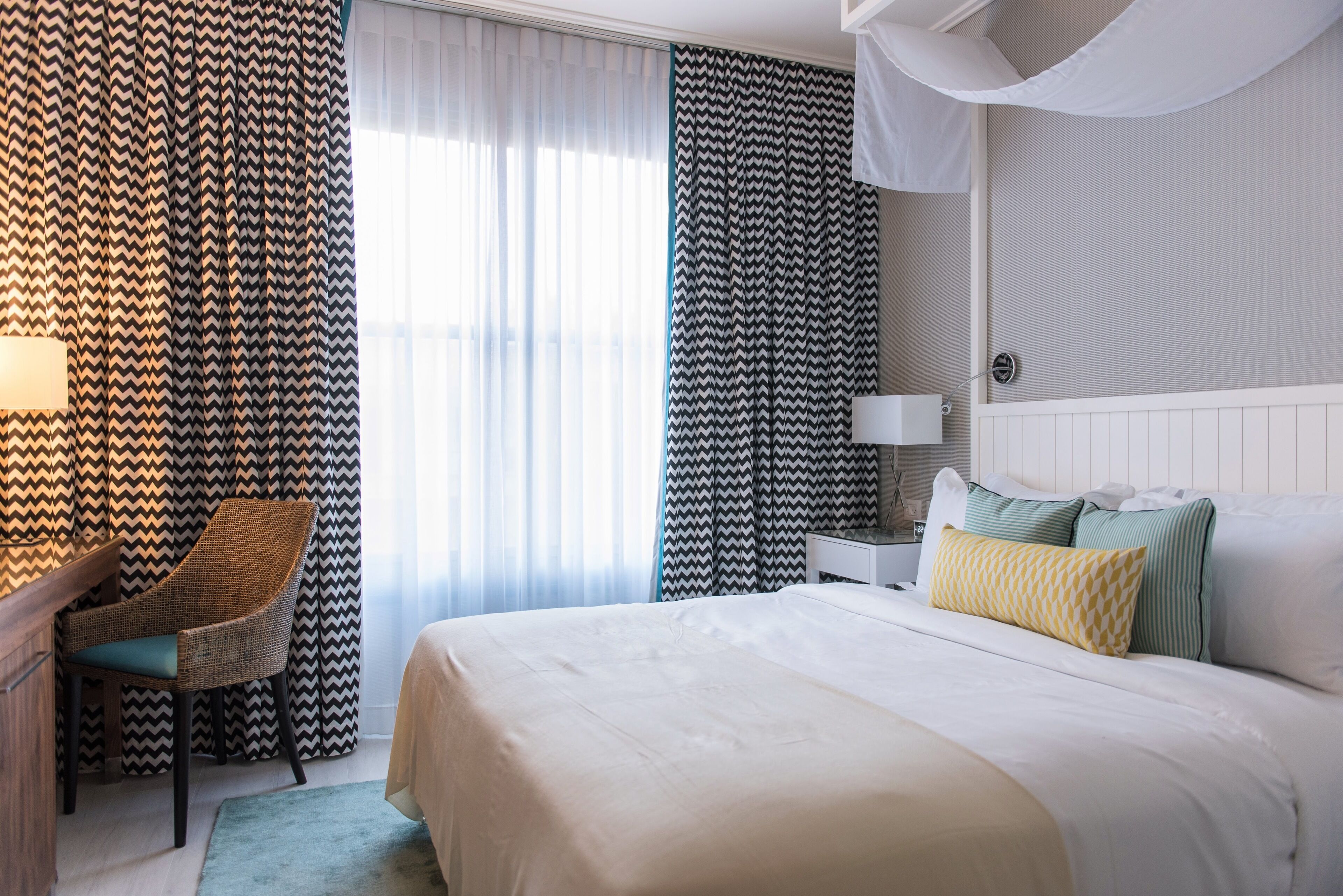 Quarto de hotel com cama, cadeira, mesa de cabeceira e cortinas.