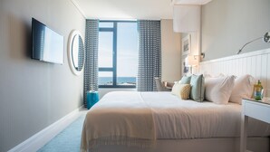 Quarto com cama grande, televisão fixada na parede e vista para o mar pela janela.