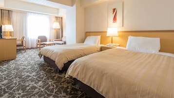 Quarto de hotel com duas camas, uma escrivaninha, uma cadeira e uma luminária.