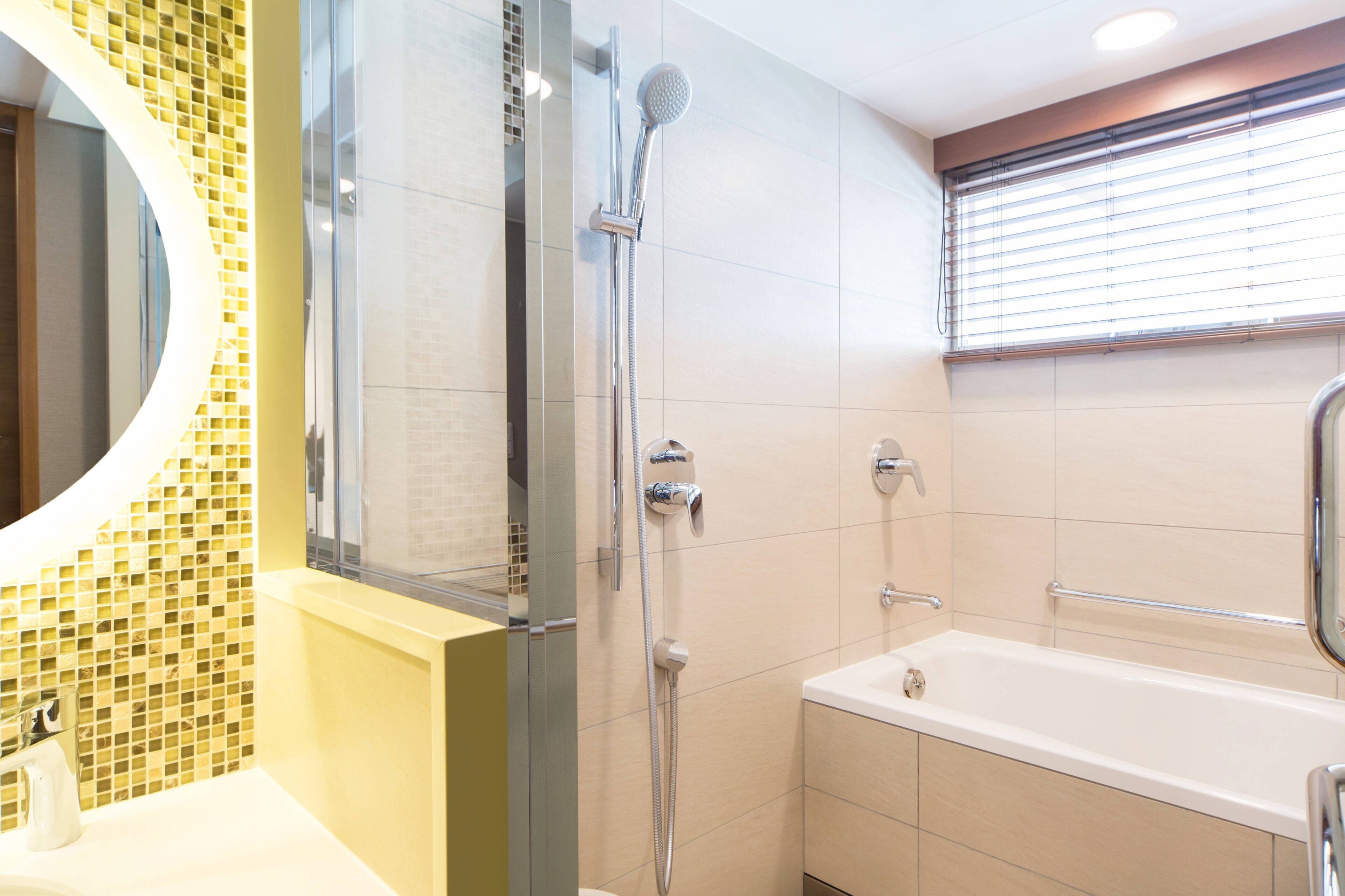 Um banheiro moderno com chuveiro em box de vidro, banheira branca e um espelho grande com mosaico amarelo no revestimento.