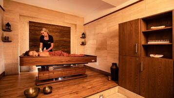 Quarto com piso de madeira, uma mesa de massagem, um armário com prateleiras e duas tigelas no chão.