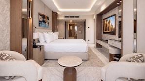 Quarto de hotel moderno com uma cama grande, televisão, escrivaninha e área de estar.
