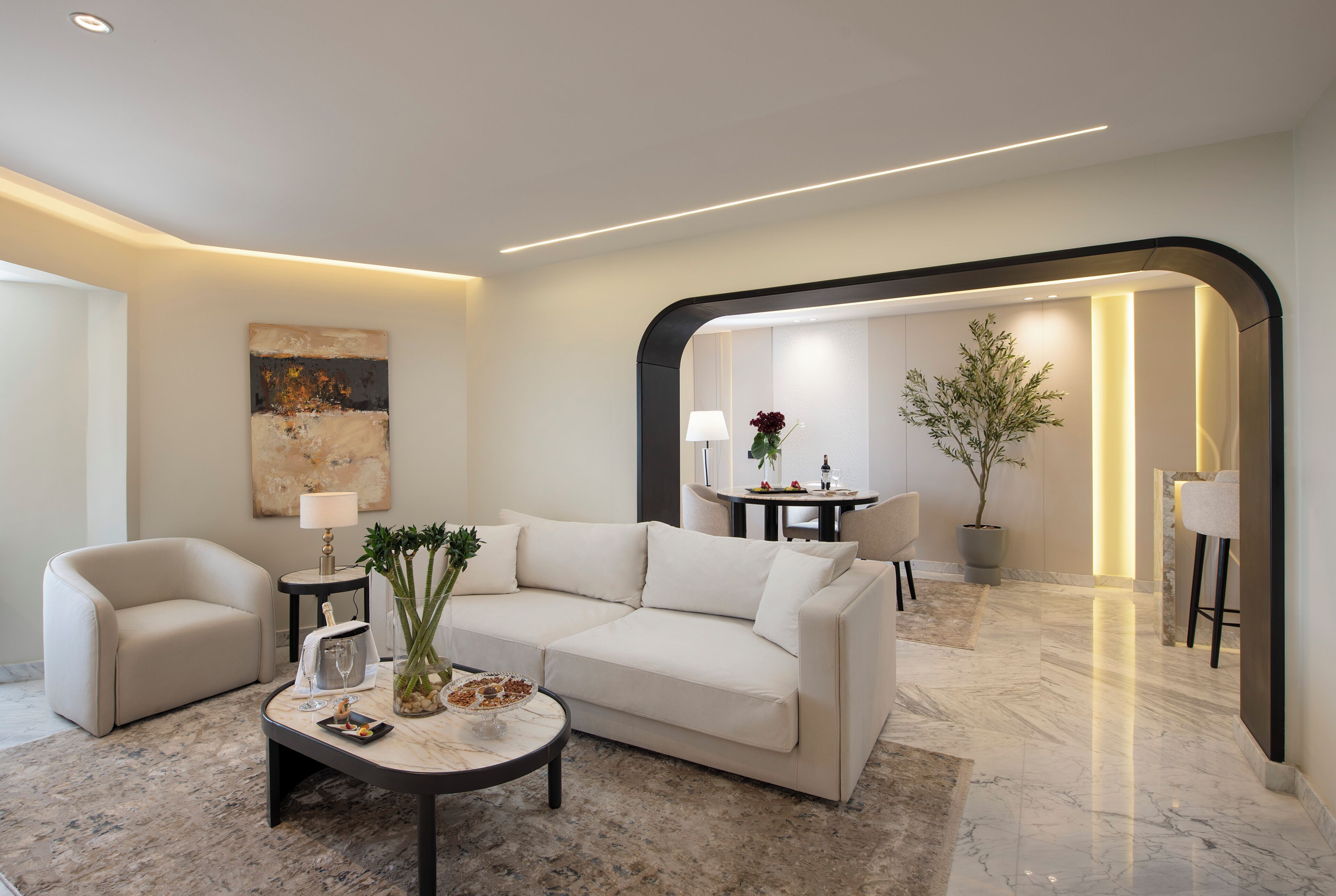 Uma sala de estar moderna com sofá, mesa de centro e poltronas. Há uma área de jantar com mesa e cadeiras.