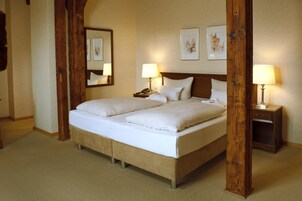 Uma cama de casal com roupa de cama branca, duas mesas de cabeceira com luminárias, e obras de arte emolduradas na parede.