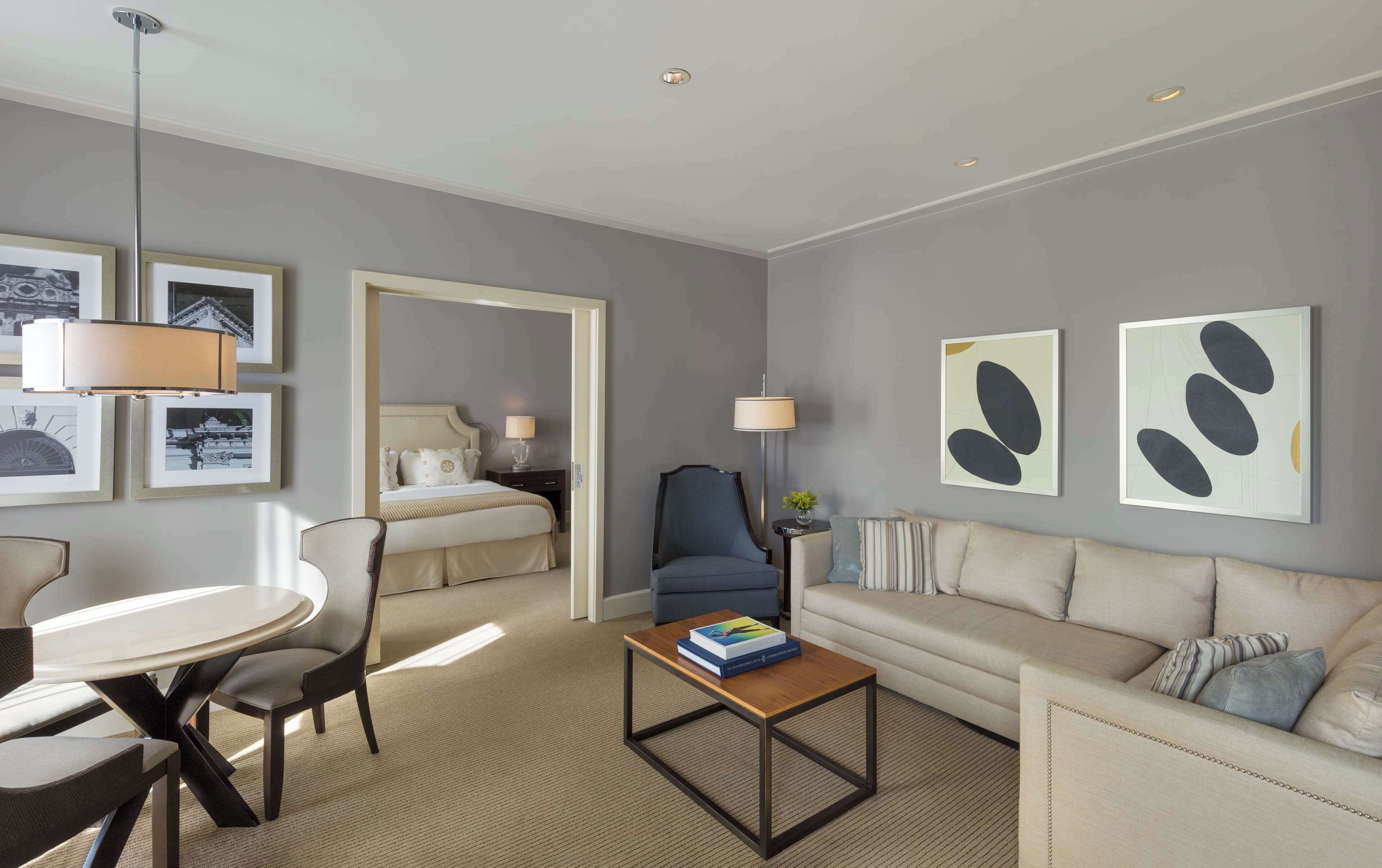 Quarto de hotel moderno com uma cama, sofá, mesa de centro, escrivaninha com cadeiras e obras de arte nas paredes.