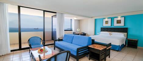 Quarto de hotel com varanda, cama, sofá, mesa de jantar e uma mesinha.