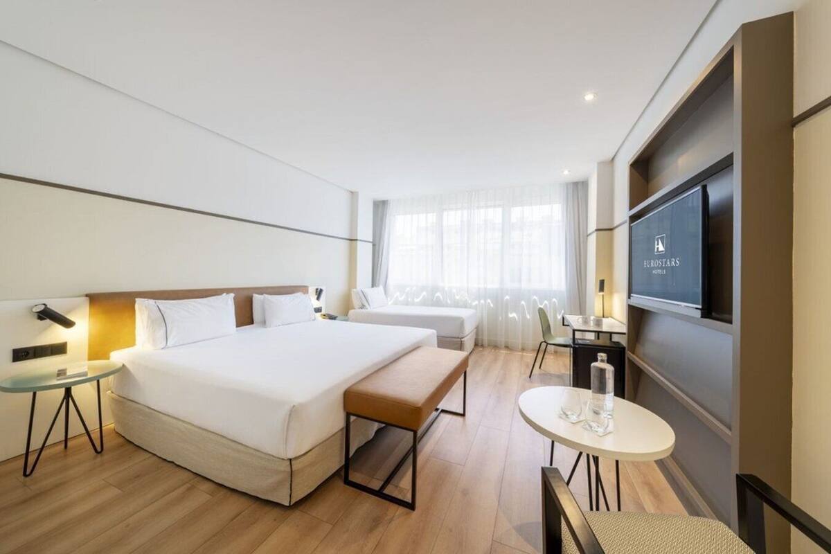 Quarto de hotel com uma cama grande, uma escrivaninha, uma cadeira e uma televisão.