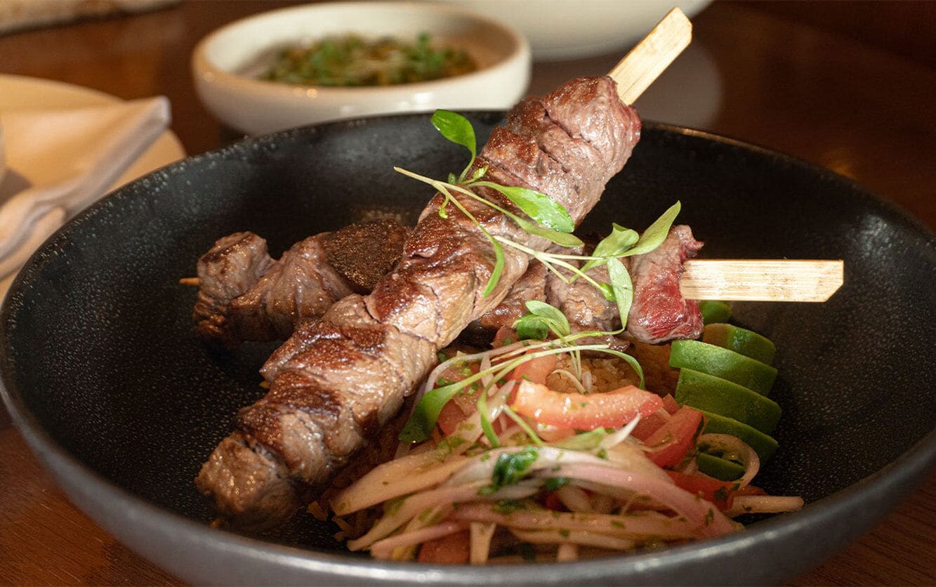 Uma tigela com espetinhos de carne, legumes e um acompanhamento.