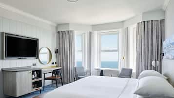 Quarto de hotel com cama, escrivaninha, cadeira, televisão e vista para o mar.