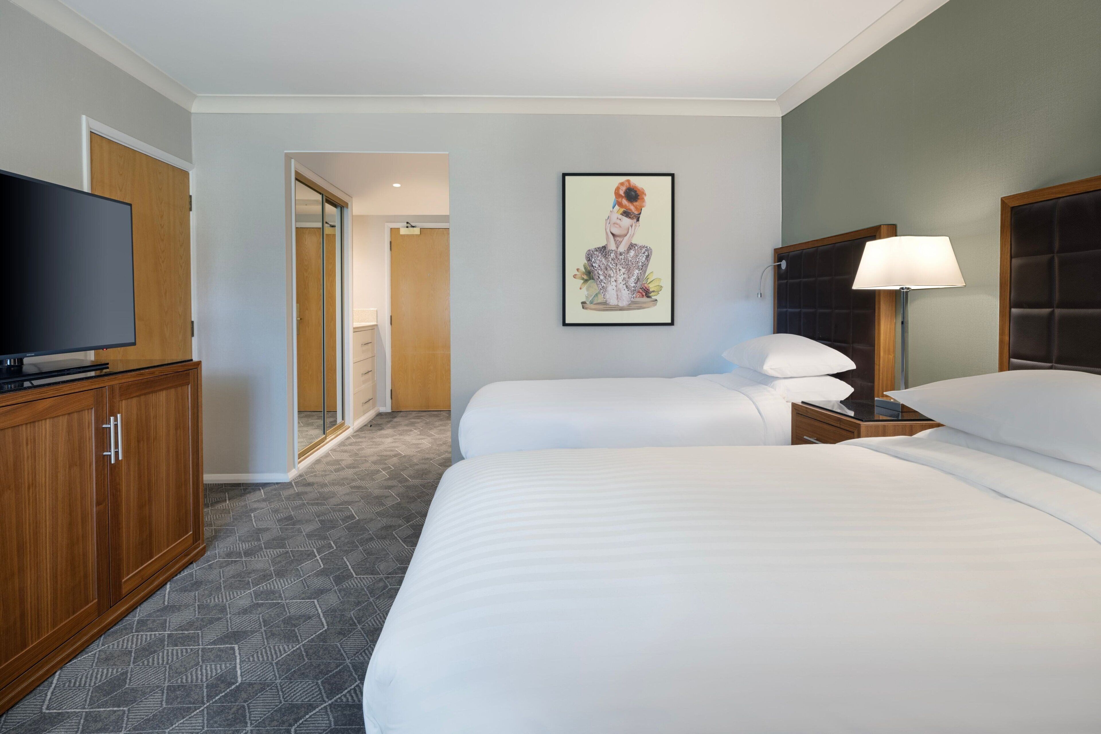 Quarto de hotel com uma cama grande, televisão, um quadro na parede e uma luminária.