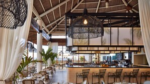 Um restaurante com área de bar, cadeiras de vime e piso estampado.