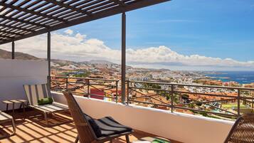 Varanda com vista para paisagem urbana costeira, uma cadeira e uma mesa.