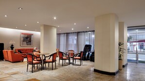 Um saguão de hotel com área de estar, um sofá, uma mesa e uma janela grande.