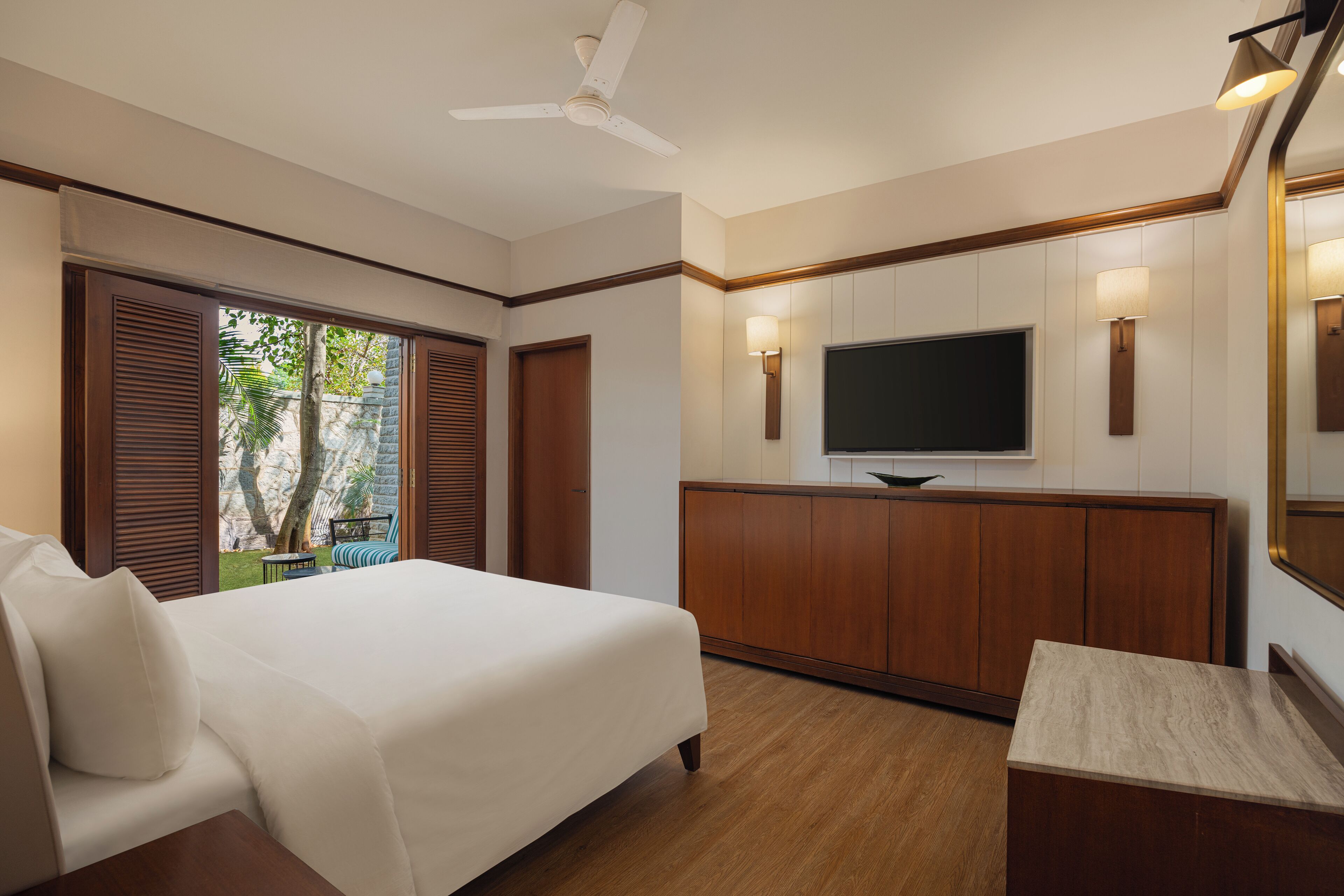 Quarto com cama, televisão, ventilador de teto e vista para o exterior.