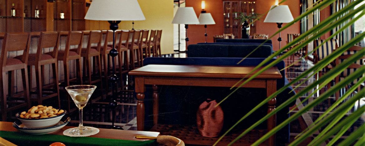 Um restaurante com cadeiras de madeira, uma mesa com uma taça de martini e uma tigela de nozes.