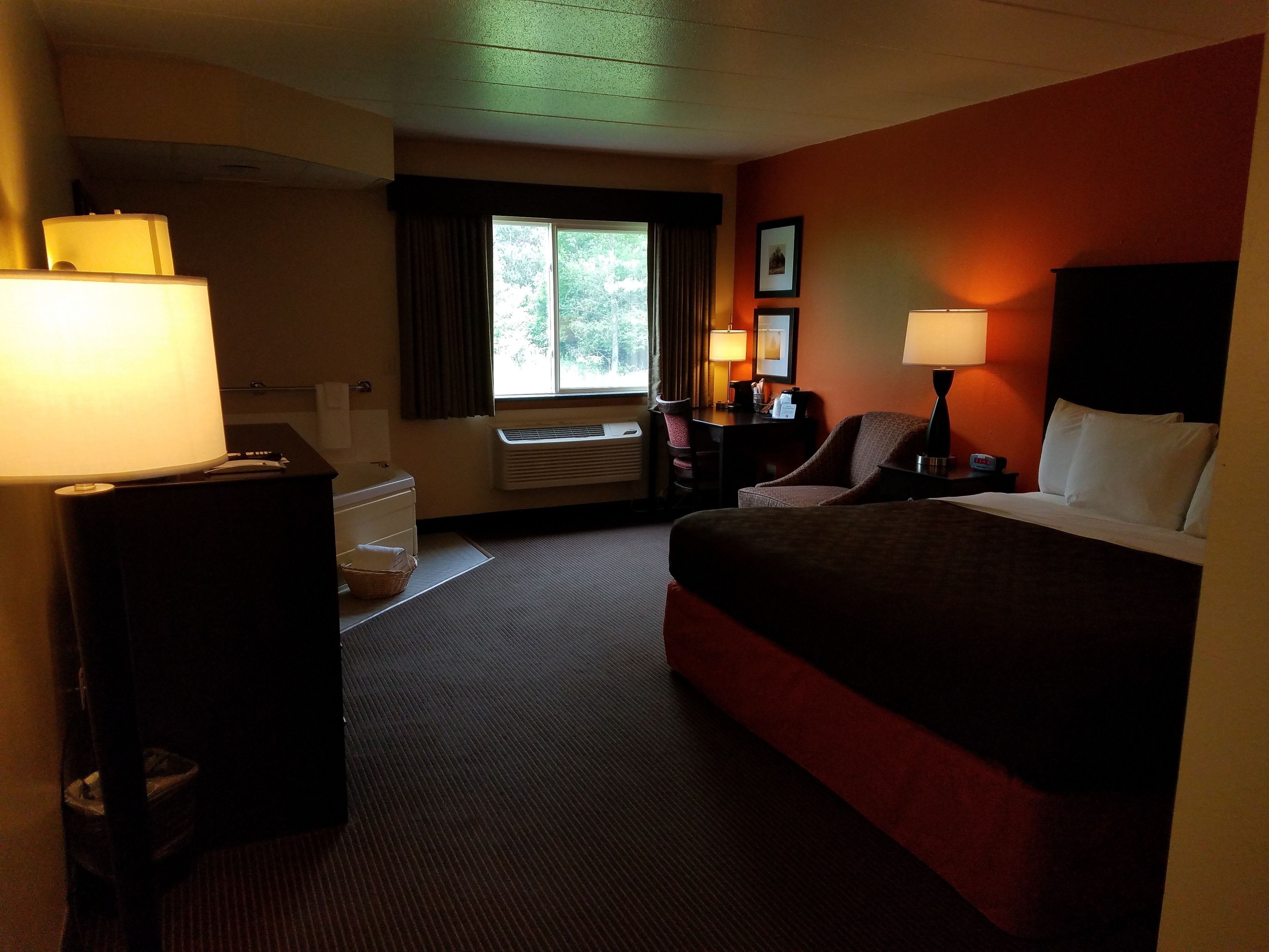 Quarto de hotel com cama, escrivaninha, cadeira, abajur e janela.