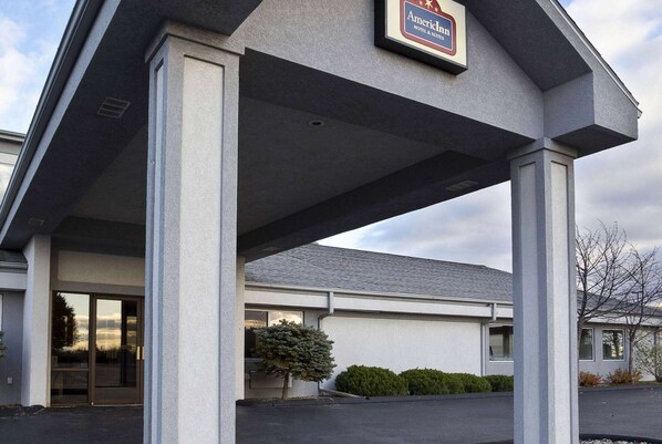 Um motel moderno com entrada coberta, placa de identificação e gramado bem cuidado.