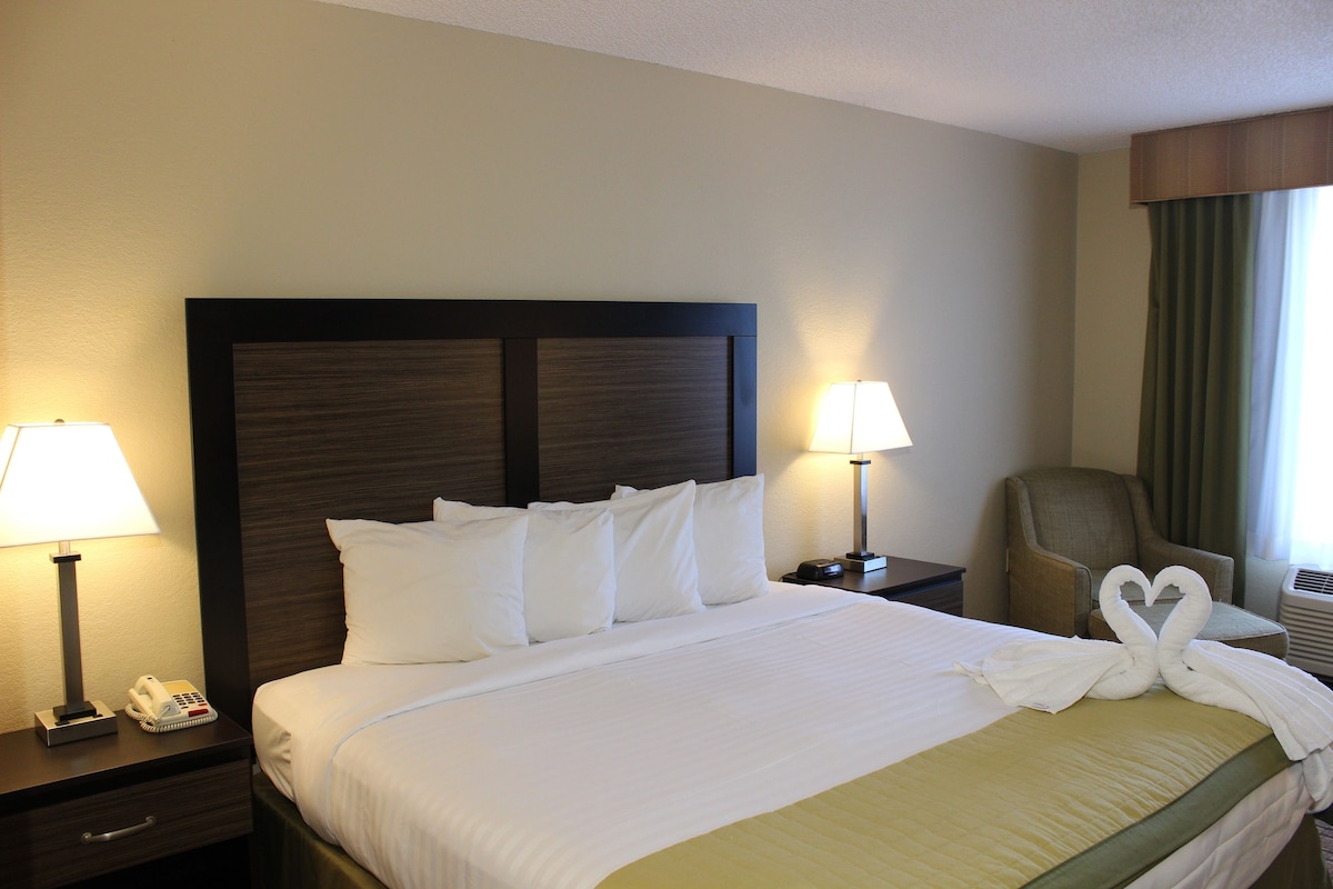 Quarto de hotel com uma cama grande, duas luminárias de cabeceira, uma cadeira e um telefone na mesinha de cabeceira.