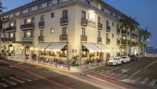 Um hotel com vários andares, varandas, área externa para sentar e vista para o mar.