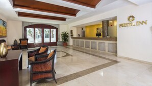Um hall com balcão de atendimento, cadeiras de vime, uma grande planta em vaso e uma placa 'Fiesta Inn'.