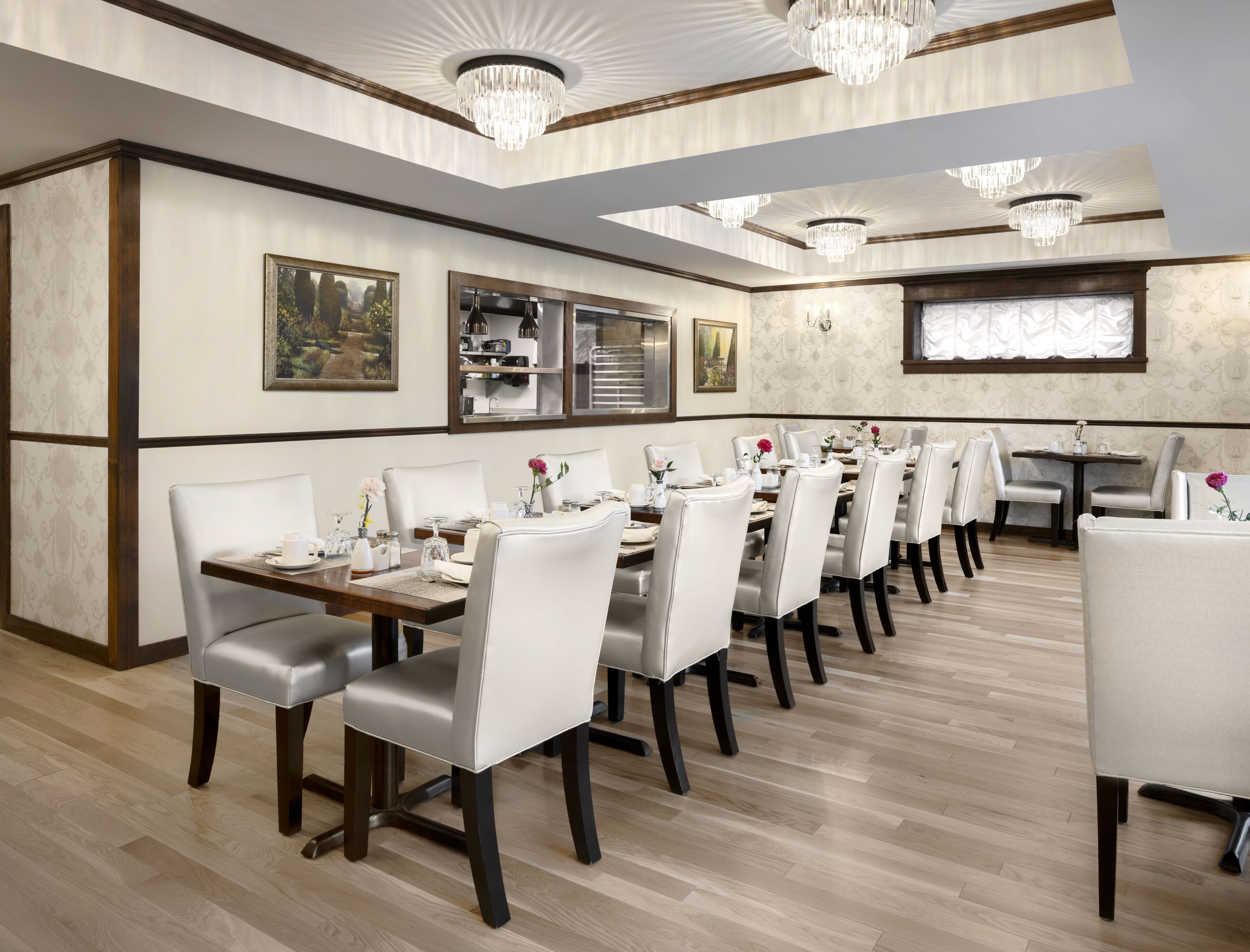 Uma sala de jantar com várias mesas e cadeiras, um candelabro e papel de parede estampado.