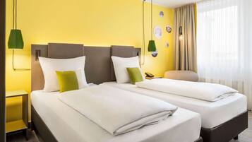 Quarto de hotel com duas camas, uma mesa de cabeceira, uma cadeira e uma janela com cortinas.