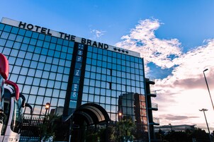 Um hotel moderno com fachada de vidro e o nome "HOTEL THE BRAND" em destaque.