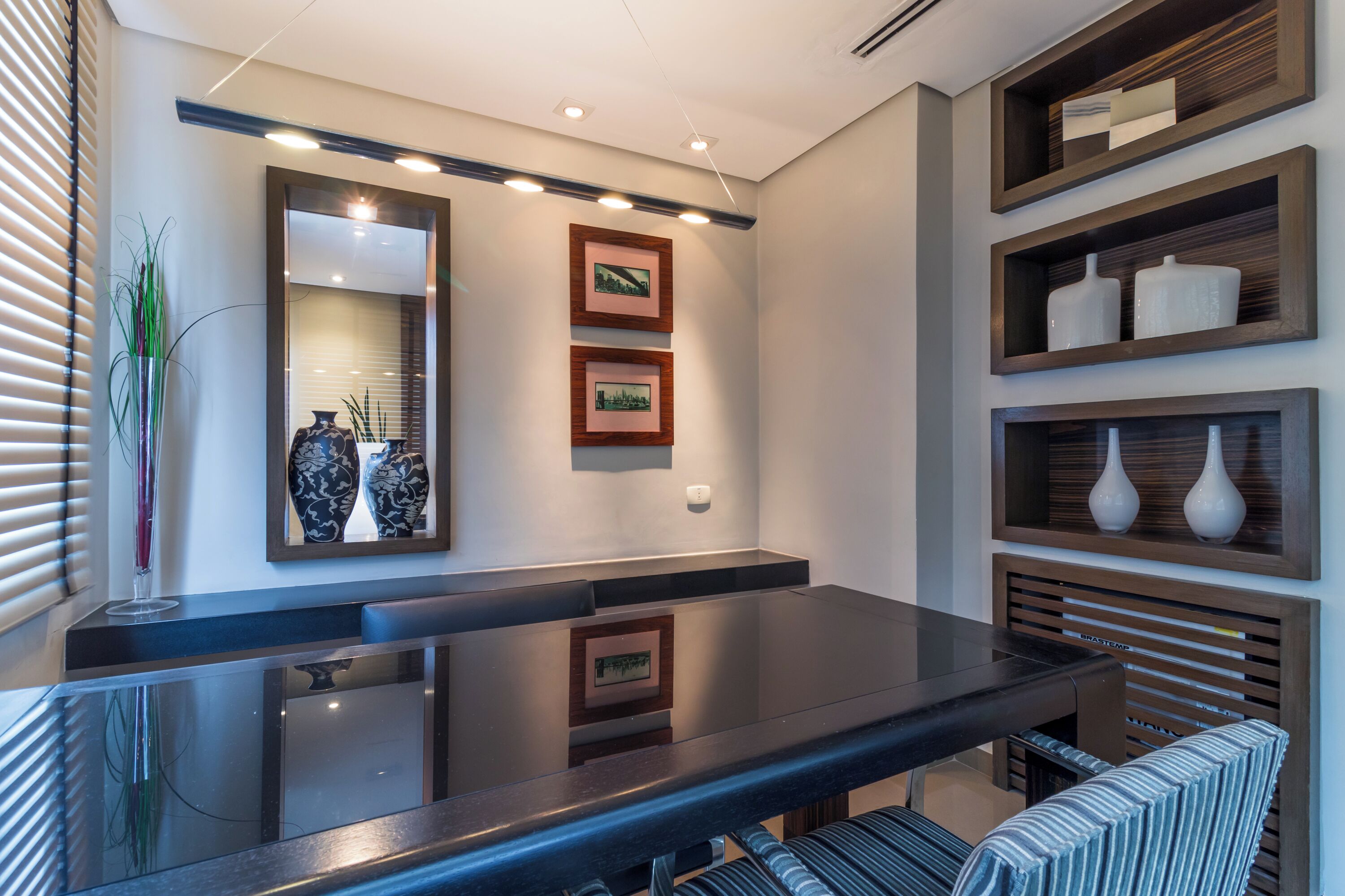 Uma sala de jantar moderna com mesa de vidro, cadeiras listradas e prateleiras de madeira com vasos decorativos.
