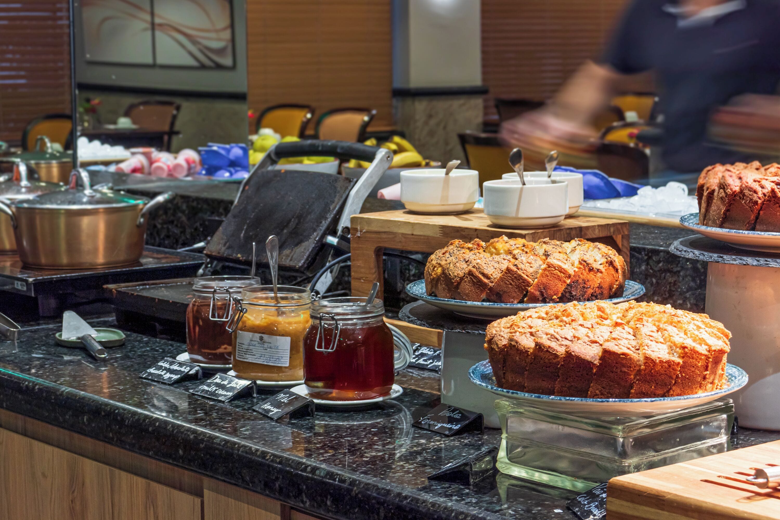 Buffet com diversos alimentos, incluindo uma barra de pão e potes de acompanhamentos.