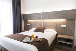 Quarto de hotel com cama, mesa de cabeceira e bandeja de café da manhã.