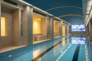Piscina interior moderna com paredes de vidro transparente, água azul e teto com claraboia.