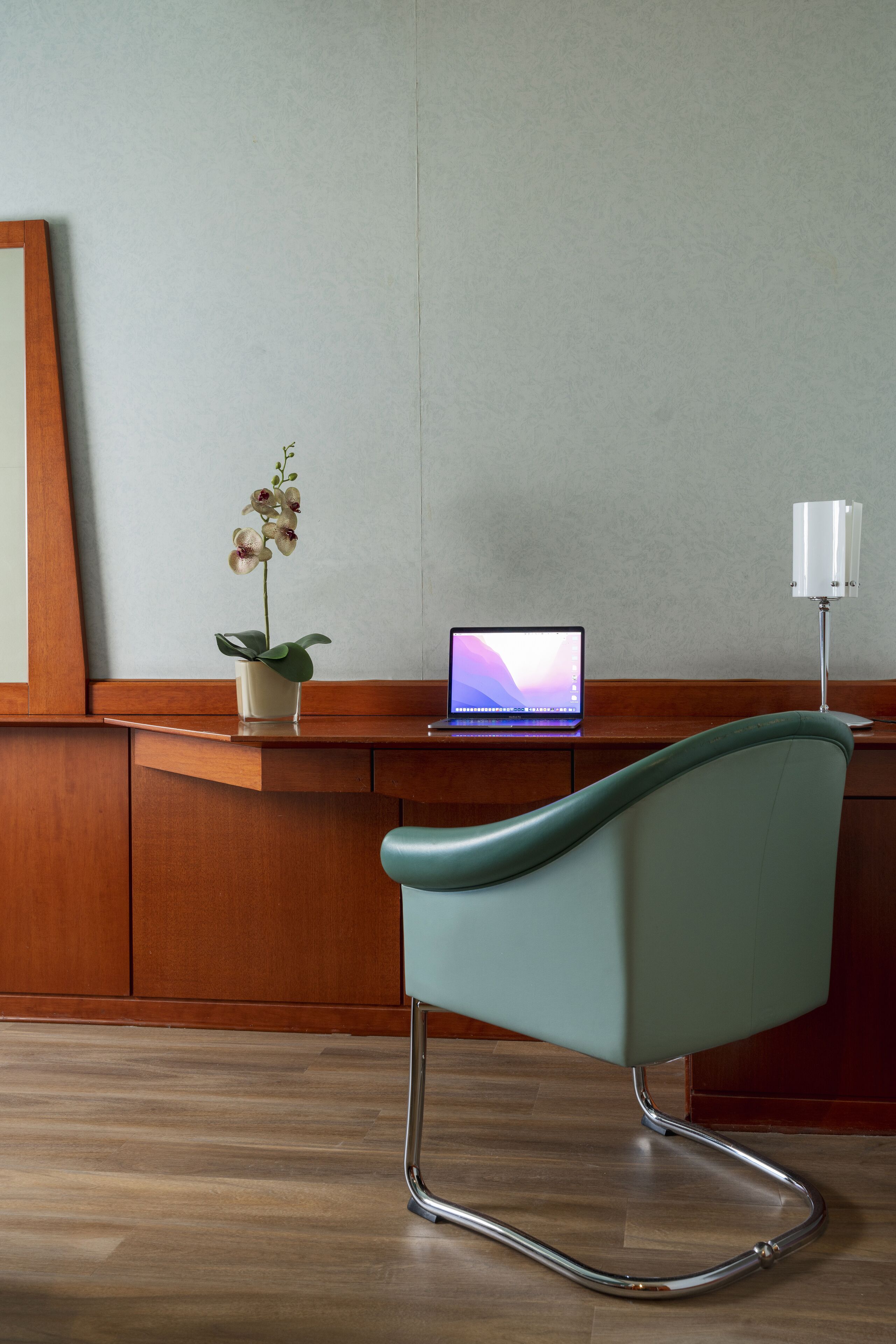 Uma mesa de escritório moderna com um laptop, uma orquídea em vaso e uma luminária de mesa.