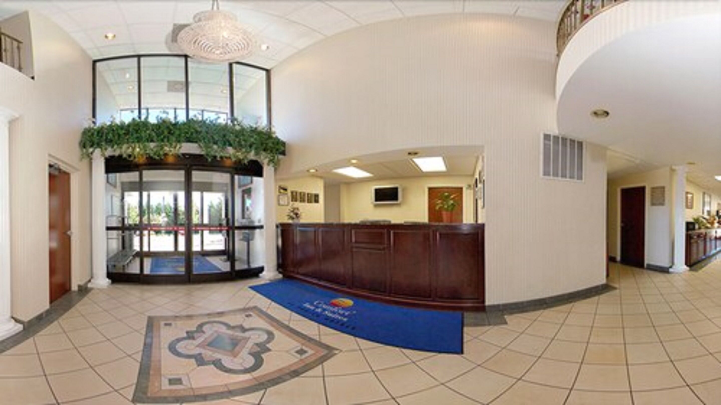 Um saguão de hotel com balcão de recepção, porta de vidro e um lustre grande, além de um piso com padrão.