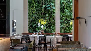 Um restaurante com teto alto, parede verde e área de estar com mesas e cadeiras.