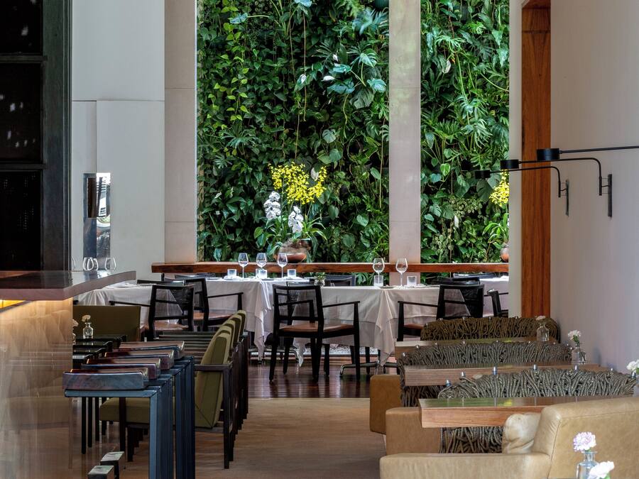 Um restaurante com teto alto, parede verde e área de estar com mesas e cadeiras.