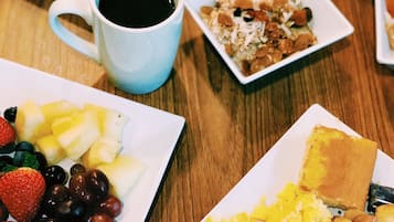 Mesa de café da manhã com diversos pratos, incluindo torradas, frutas, ovos mexidos, bacon e uma xícara de café.