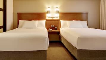 Quarto de hotel com duas camas de solteiro, cabeceira de madeira, abajures e uma mesinha com telefone e garrafa.