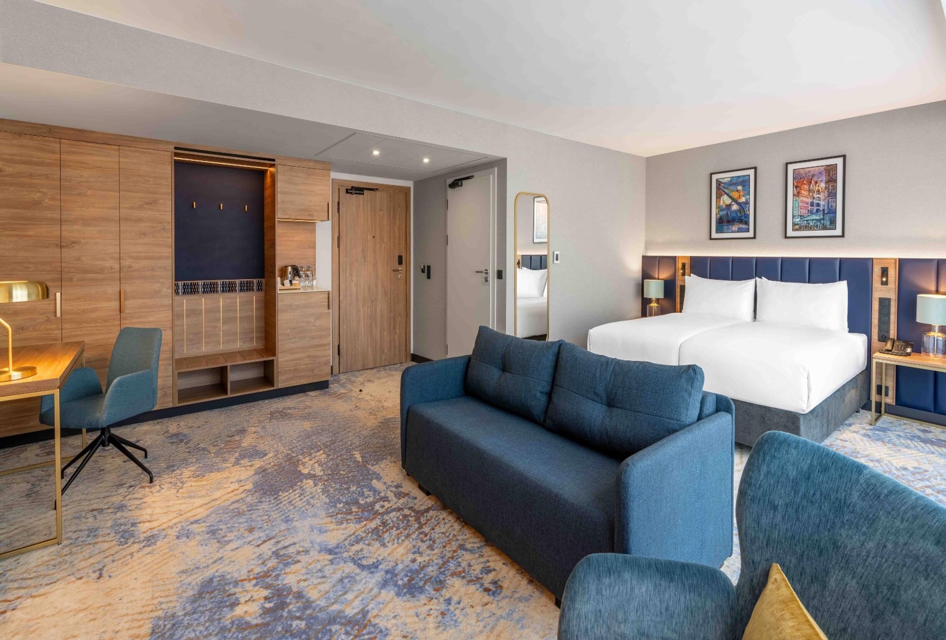 Quarto de hotel com cama, sofá, escrivaninha e guarda-roupa.