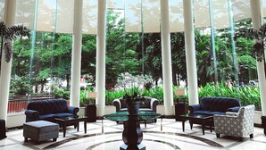 Um hall espaçoso com uma mesa redonda central, disposição de assentos e amplas janelas com vista para o verde lá fora.