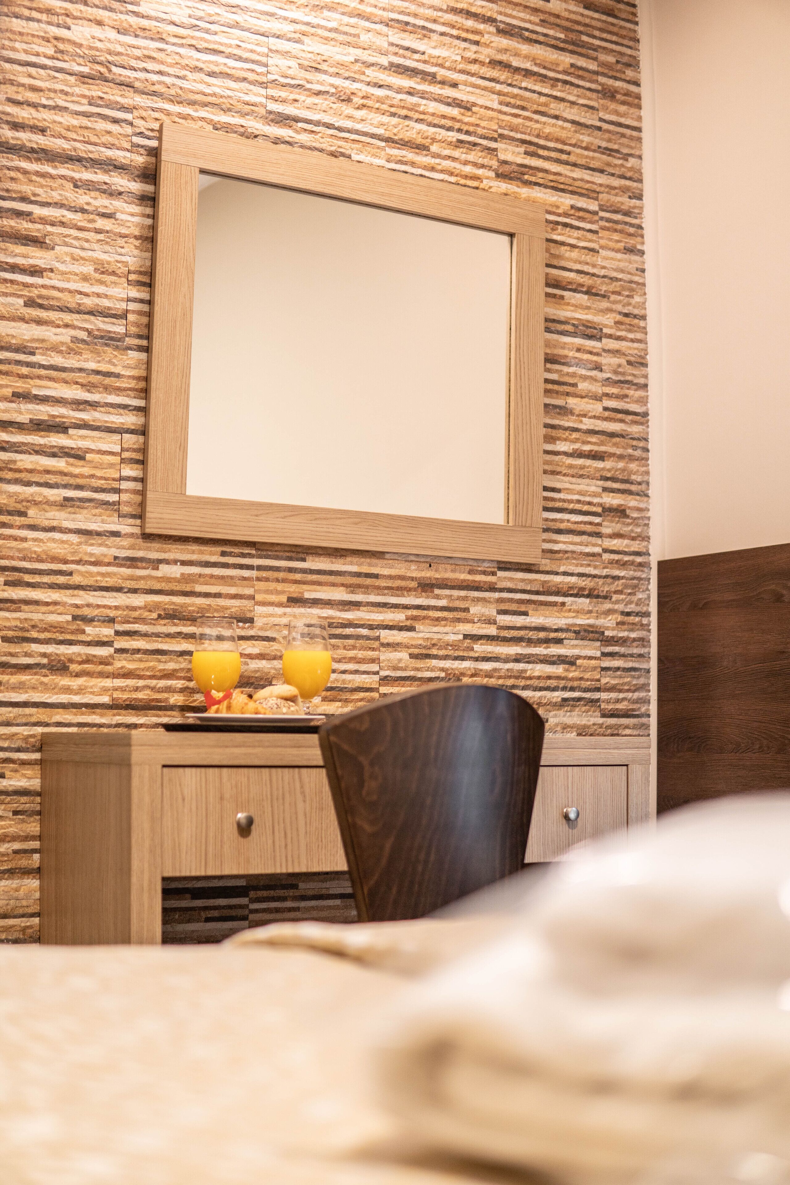 Quarto de hotel com cabeceira de madeira, mesa de cabeceira de madeira com espelho e cama com colcha branca.