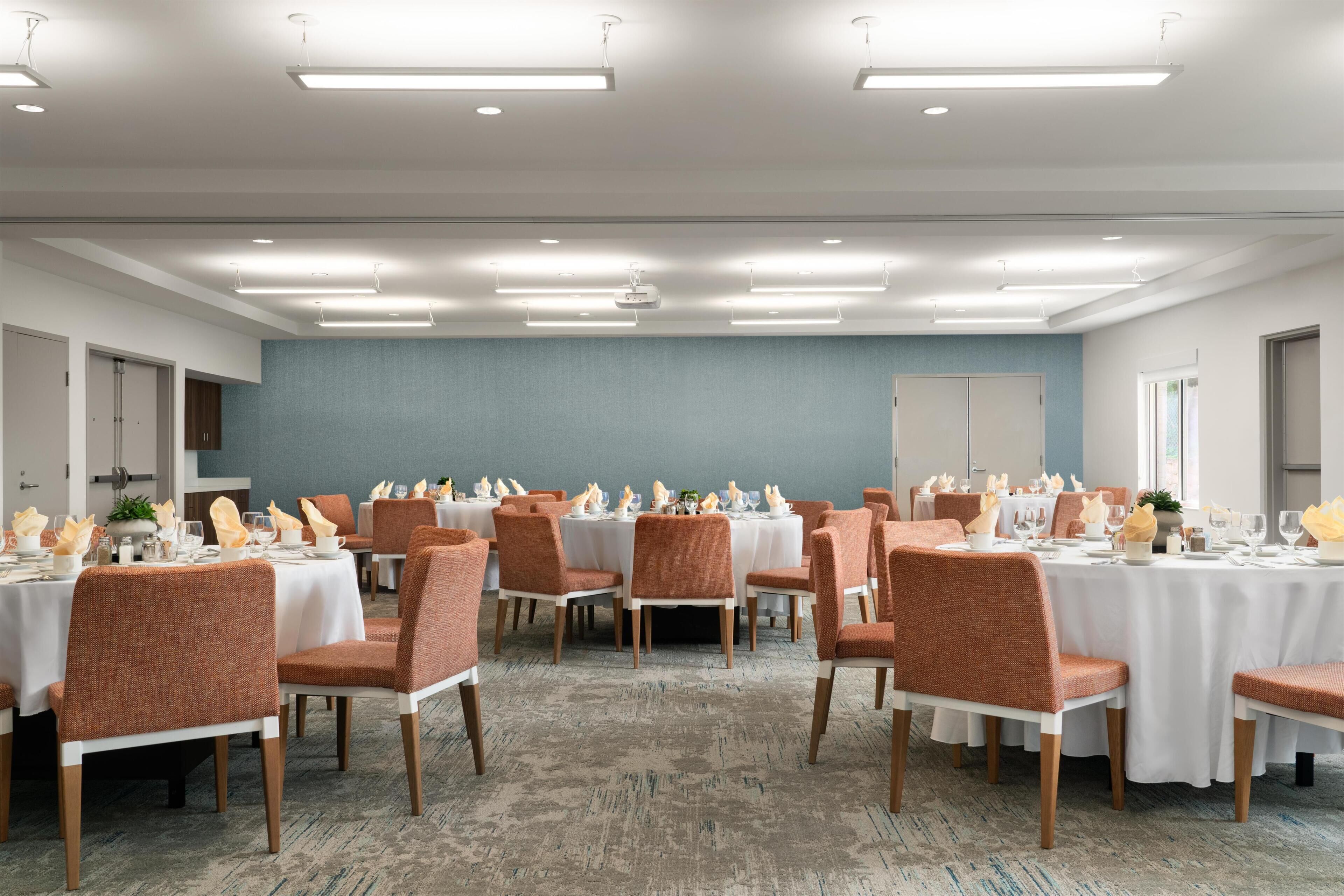 Sala de conferências com várias mesas, cadeiras e uma parede azul como destaque.