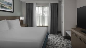 Quarto de hotel com cama, televisão, escrivaninha e janela com cortinas.