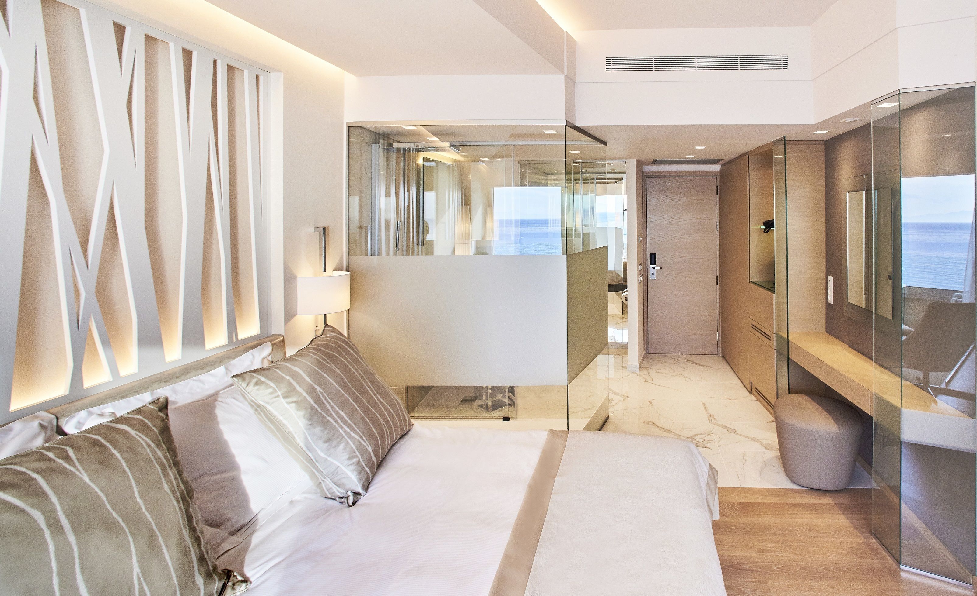Quarto de hotel moderno com uma cama grande, divisória de vidro, televisão e vista para o mar.