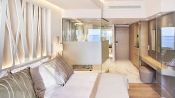 Quarto de hotel moderno com uma cama grande, divisória de vidro, televisão e vista para o mar.