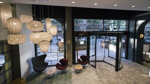 Um lobby moderno com uma porta giratória, cadeiras vermelhas e luminárias pendentes.